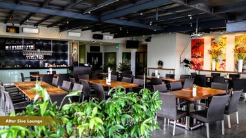 Um lounge moderno com mesas de madeira e cadeiras de vime preto, área de bar e arte decorativa nas paredes.