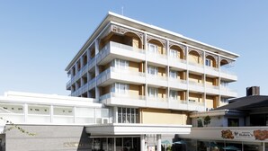 Um hotel de vários andares com entrada central, área de estar ao ar livre e uma padaria no andar térreo.