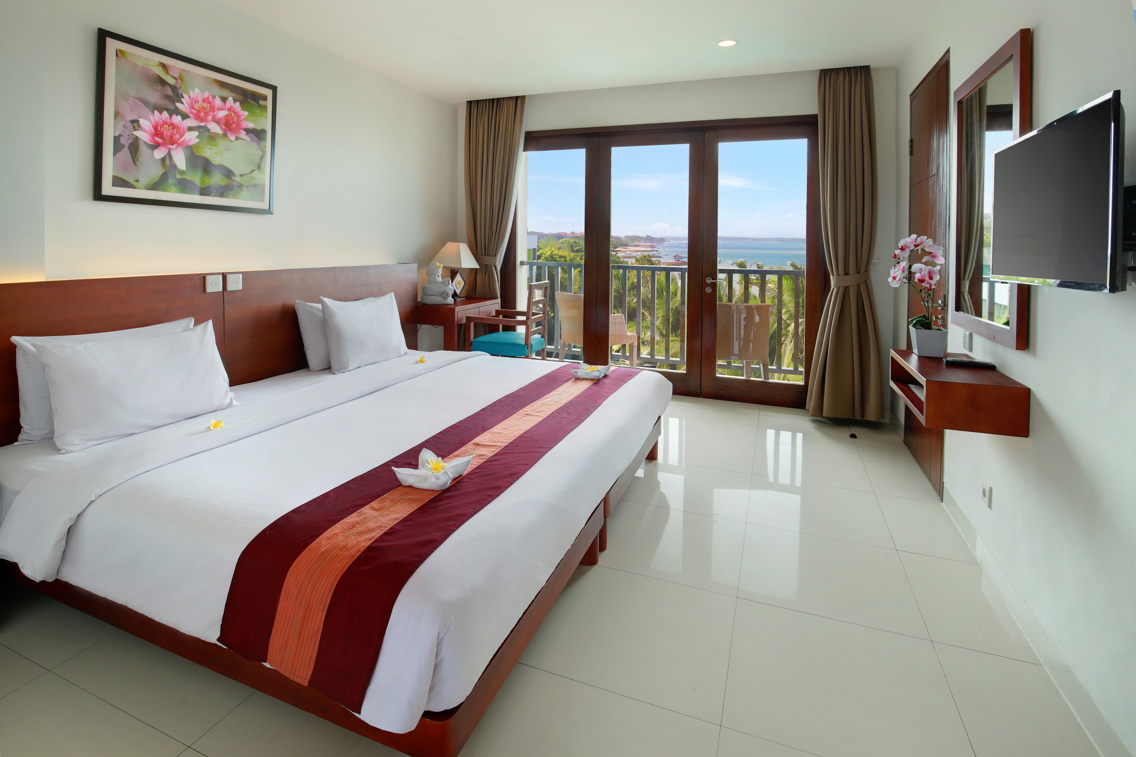 Quarto de hotel com uma cama grande, uma escrivaninha, uma cadeira, uma televisão e uma varanda com vista.