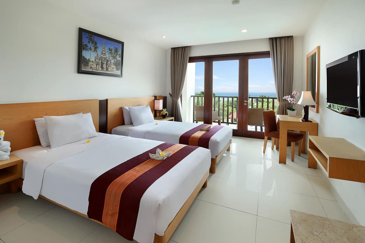 Quarto de hotel com duas camas, uma mesa, uma cadeira, televisão e varanda com vista.