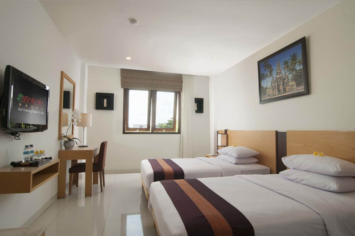 Quarto de hotel com duas camas, uma escrivaninha com cadeira, televisão e janela com cortinas.