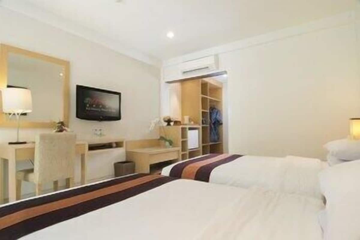 Quarto de hotel com cama, escrivaninha, cadeira, espelho, televisão e guarda-roupa.
