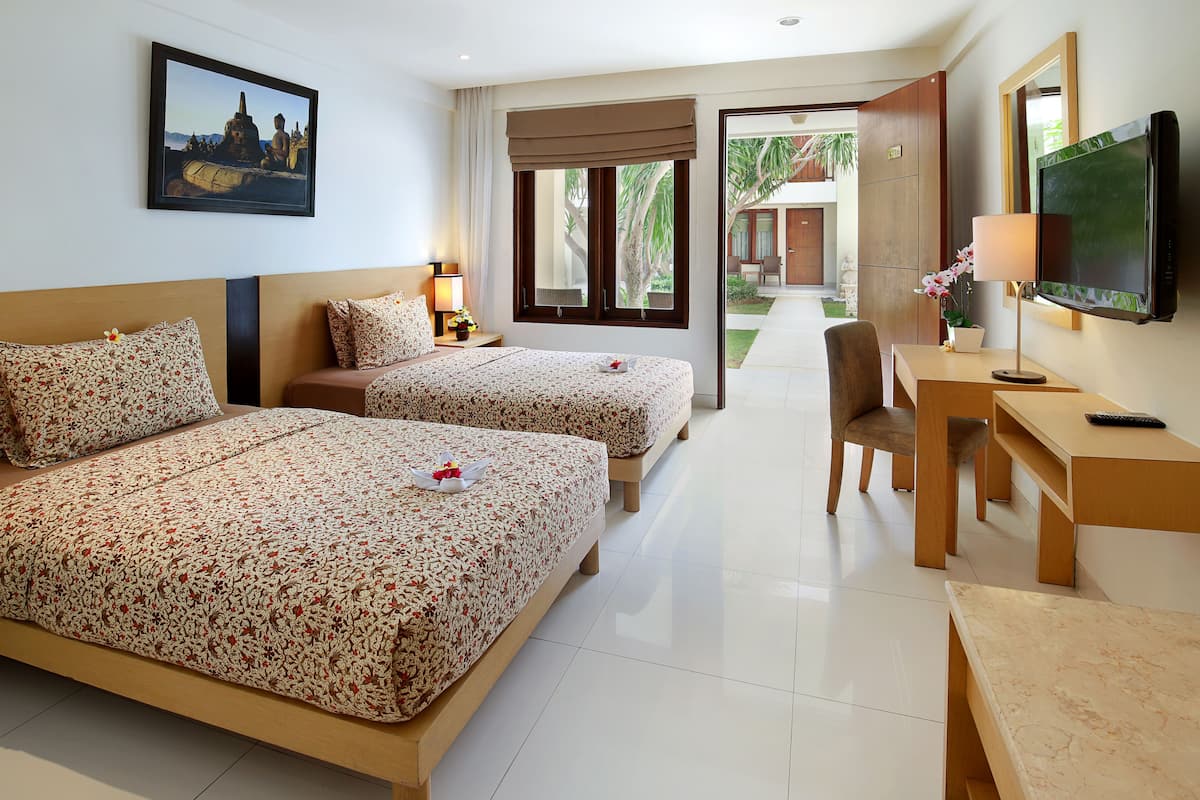 Quarto de hotel com duas camas, uma escrivaninha, uma cadeira, uma televisão e uma janela grande.