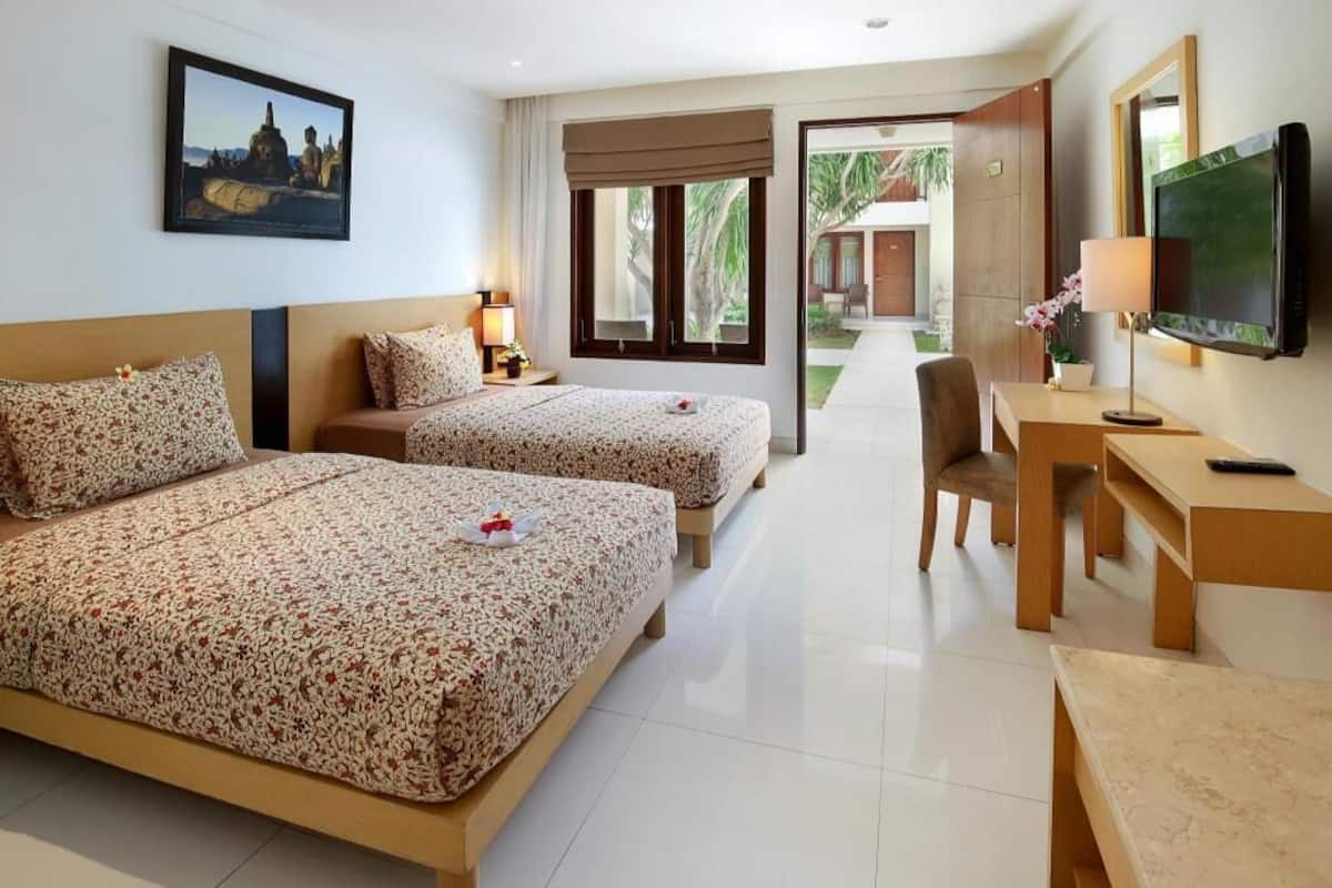 Quarto de hotel com duas camas, uma escrivaninha, uma televisão e uma janela com vista para o exterior.