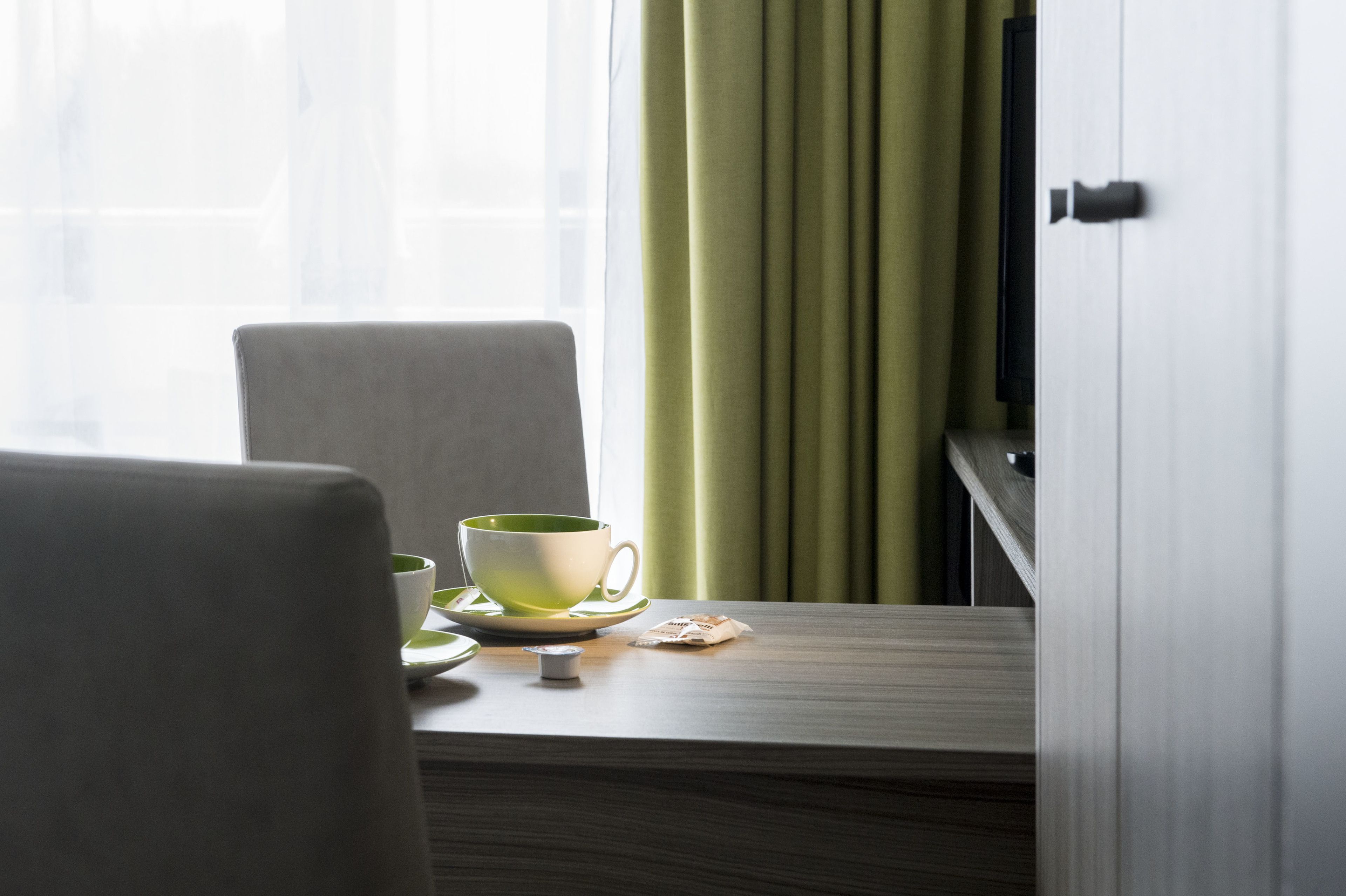 Quarto com mesa posta para dois, cortina verde e armário.