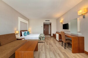 Quarto de hotel com cama, sofá, escrivaninha e televisão.