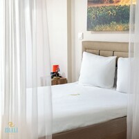 Quarto de hotel com cama, mesa de cabeceira, abajur e um quadro na parede.