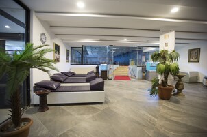 Um lobby moderno com um sofá modular, plantas em vasos e uma escada que dá acesso aos andares superiores.