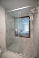 Um banheiro moderno com chuveiro em box de vidro, piso de mármore e porta-toalhas com toalhas.
