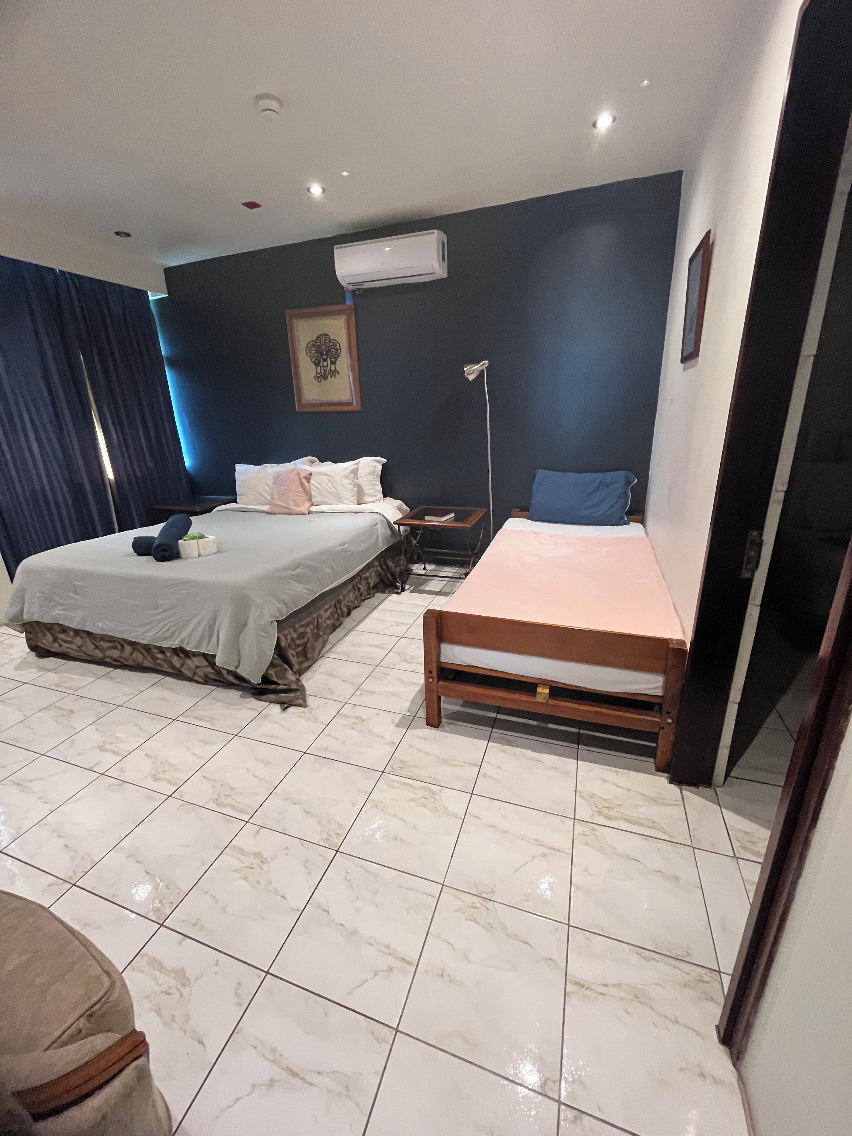 Quarto de hotel com duas camas, uma mesinha de cabeceira, um abajur e um ar condicionado fixado na parede.