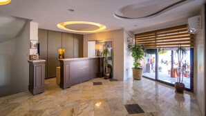 Uma área de recepção moderna com piso de mármore, balcão de madeira e uma grande planta em vaso.