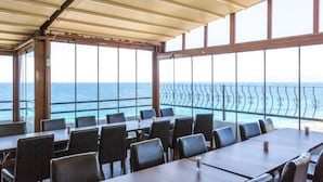 Restaurante com grandes janelas que oferecem vista para o oceano. Mesas dispostas sob uma área coberta.