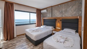 Quarto de hotel com duas camas, uma janela grande com cortinas, ar condicionado fixado na parede e um padrão decorativo de folhas na parede.