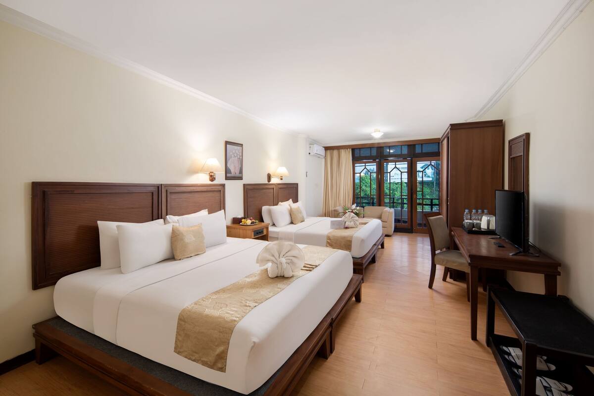 Quarto de hotel com duas camas, uma escrivaninha, televisão e vista para o exterior.