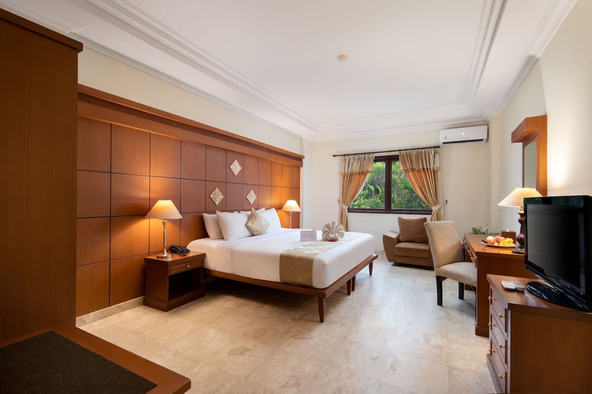 Quarto de hotel com uma cama grande, uma escrivaninha com televisão, uma cadeira e uma janela com cortinas.