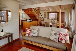 Uma sala de estar aconchegante com um sofá de madeira, uma mesa de jantar e uma escada que leva a outro andar.