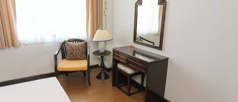 Quarto de hotel com cama, escrivaninha com luminária, cadeira e um espelho grande.
