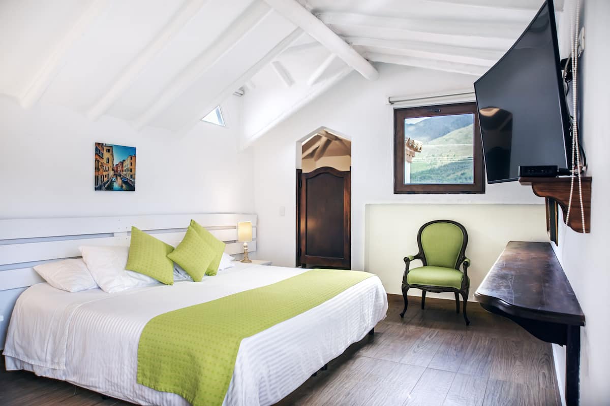 Quarto com cama, poltrona, televisão e um quadro na parede.