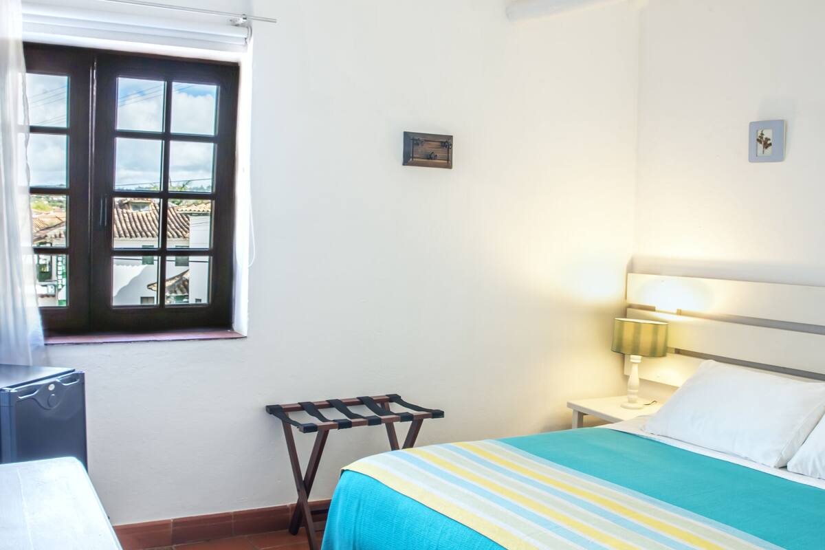 Quarto de hotel com cama, mesa de cabeceira, mesa e cadeira.