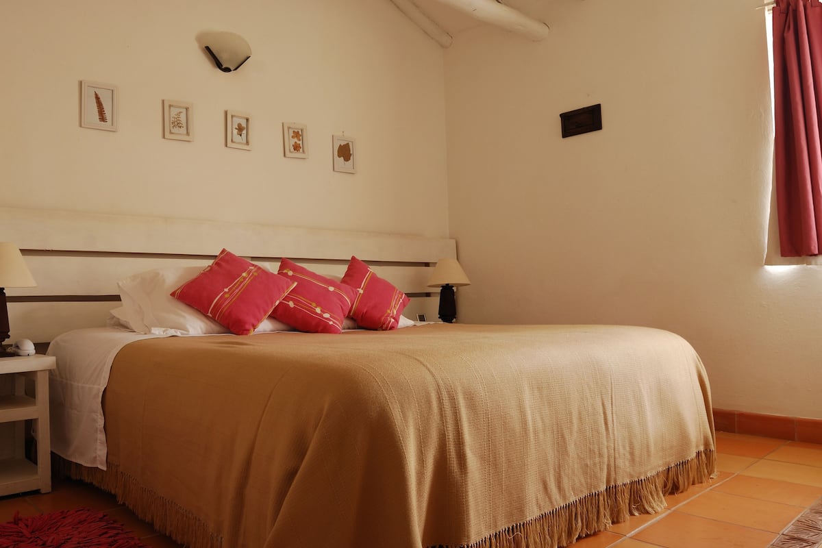Quarto com cama, mesa de cabeceira, luminária e obra de arte na parede.