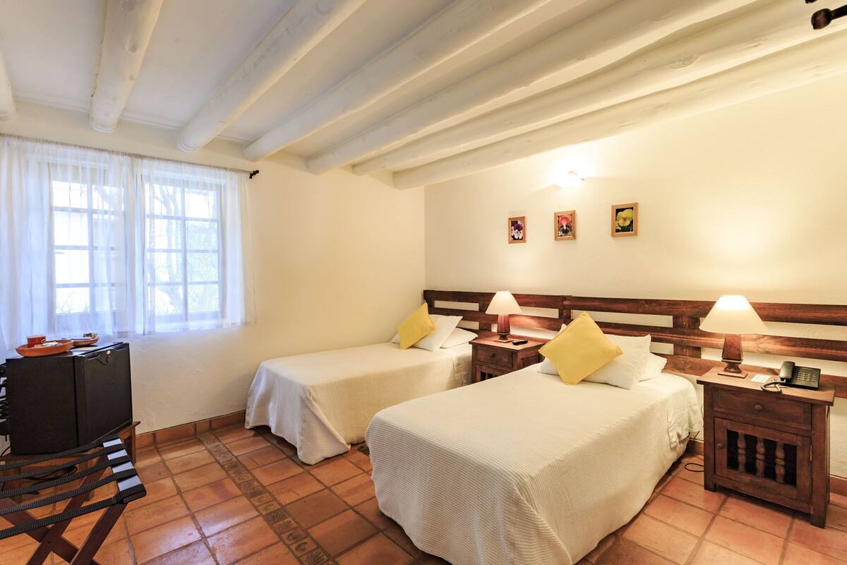 Quarto com duas camas, cabeceira de madeira, mesinha com abajur e televisão.