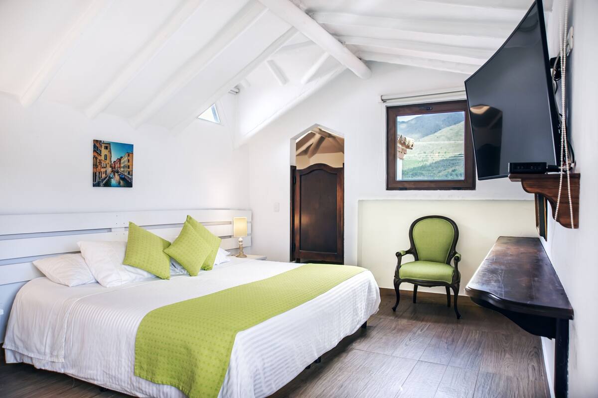 Quarto com cama, uma cadeira, televisão e um quadro na parede.