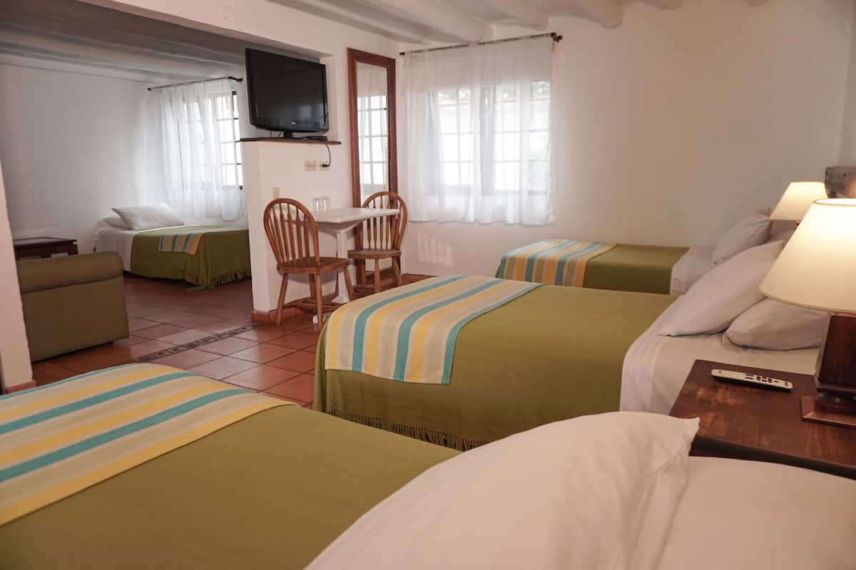 Quarto de hotel com duas camas de solteiro, um sofá, uma mesinha e uma televisão presa à parede.