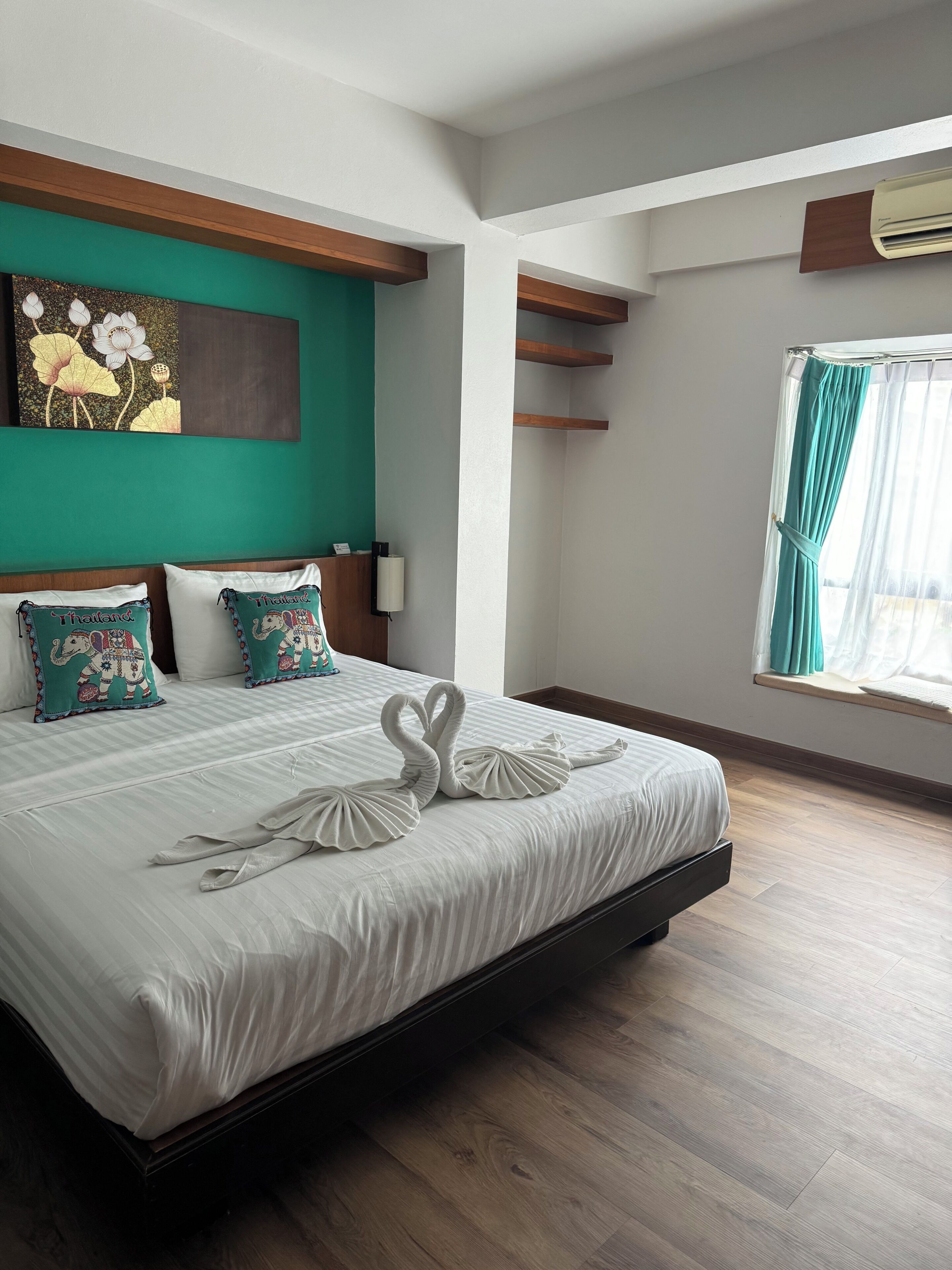 Quarto de hotel com uma cama grande, parede verde decorativa, janela com cortinas e ar condicionado fixado na parede.