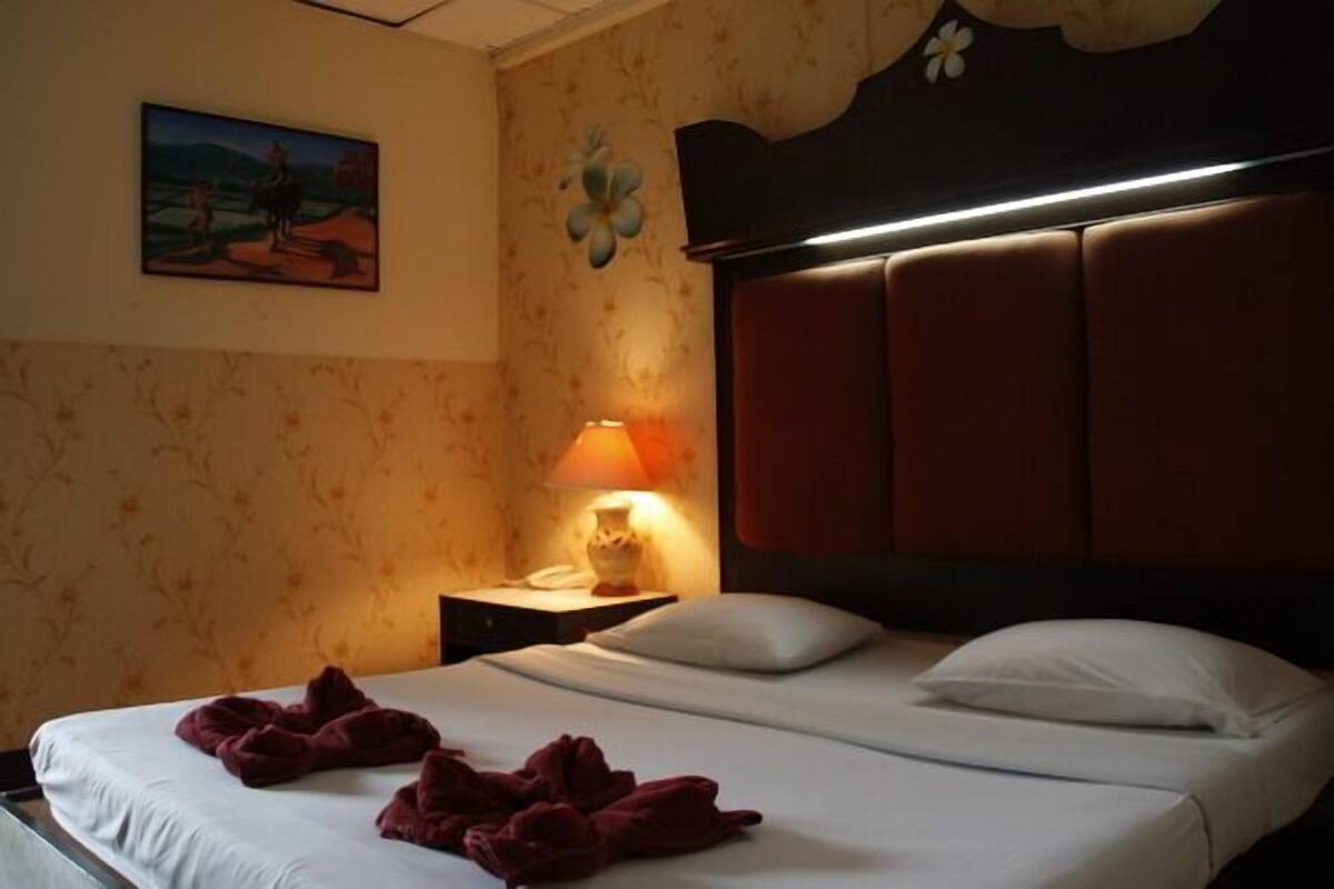 Quarto de hotel com uma cama, uma mesa de cabeceira com luminária e um design floral na parede.