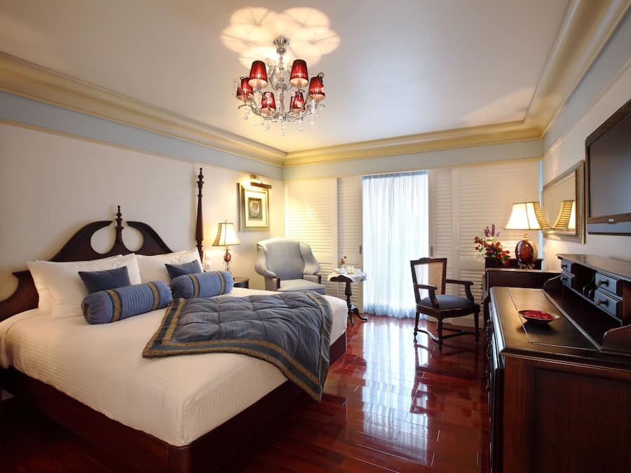 Quarto de hotel com uma cama grande, uma escrivaninha, uma cadeira, uma televisão e um lustre.