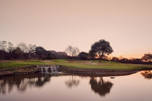 Um campo de golfe tranquilo com lago, árvores e uma pequena cascata.