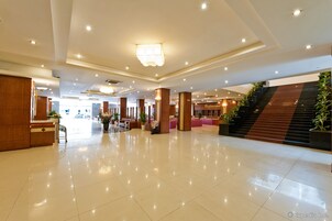 Um hall amplo com piso lustroso, um balcão de recepção e uma escadaria que dá acesso a uma área de restaurante.