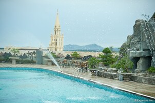 Piscina com uma fonte de água, área de estar externa e vista para um edifício histórico ao fundo.