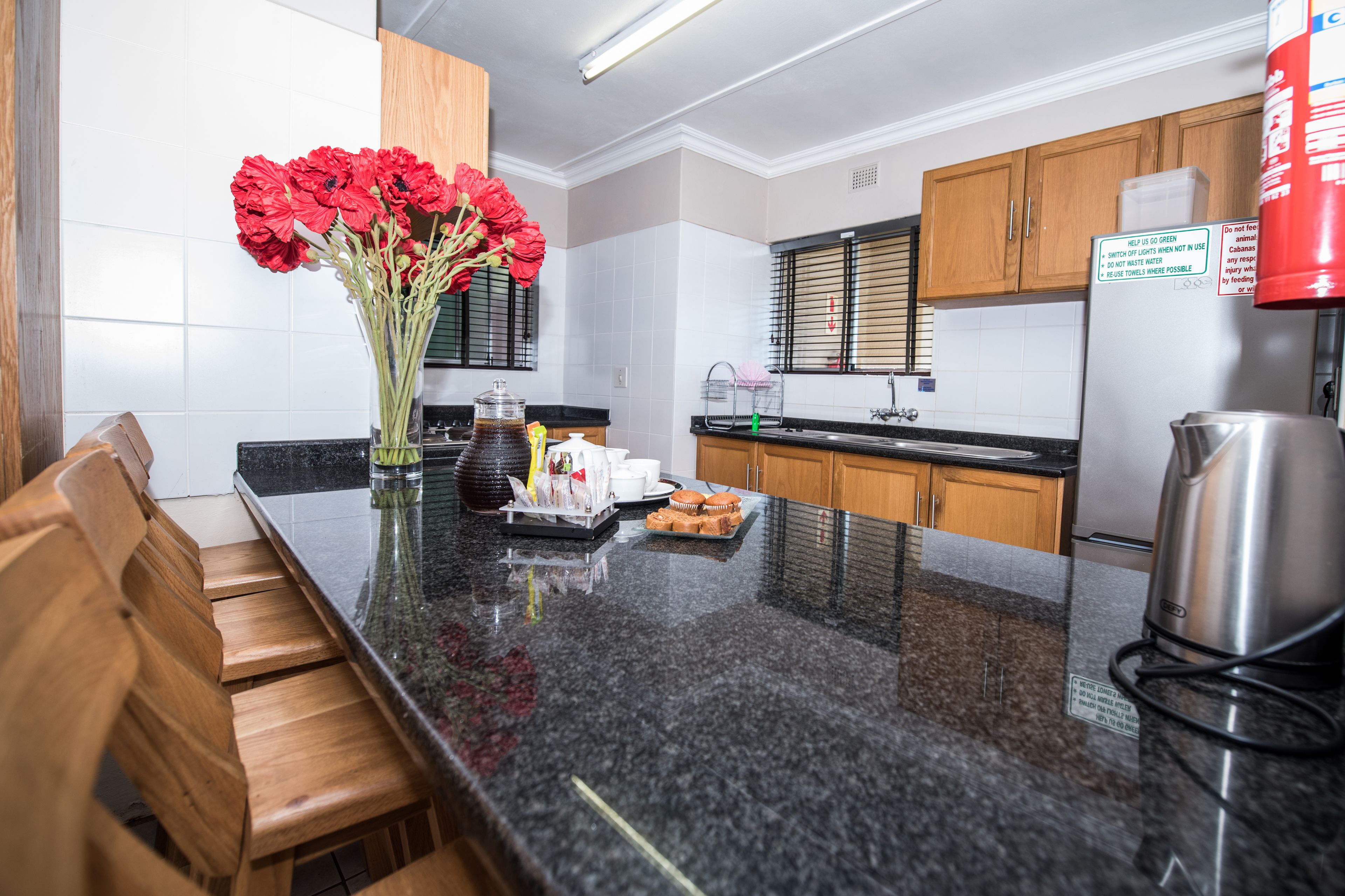 Uma cozinha moderna com armários de madeira, bancada de granito e um vaso com flores vermelhas.