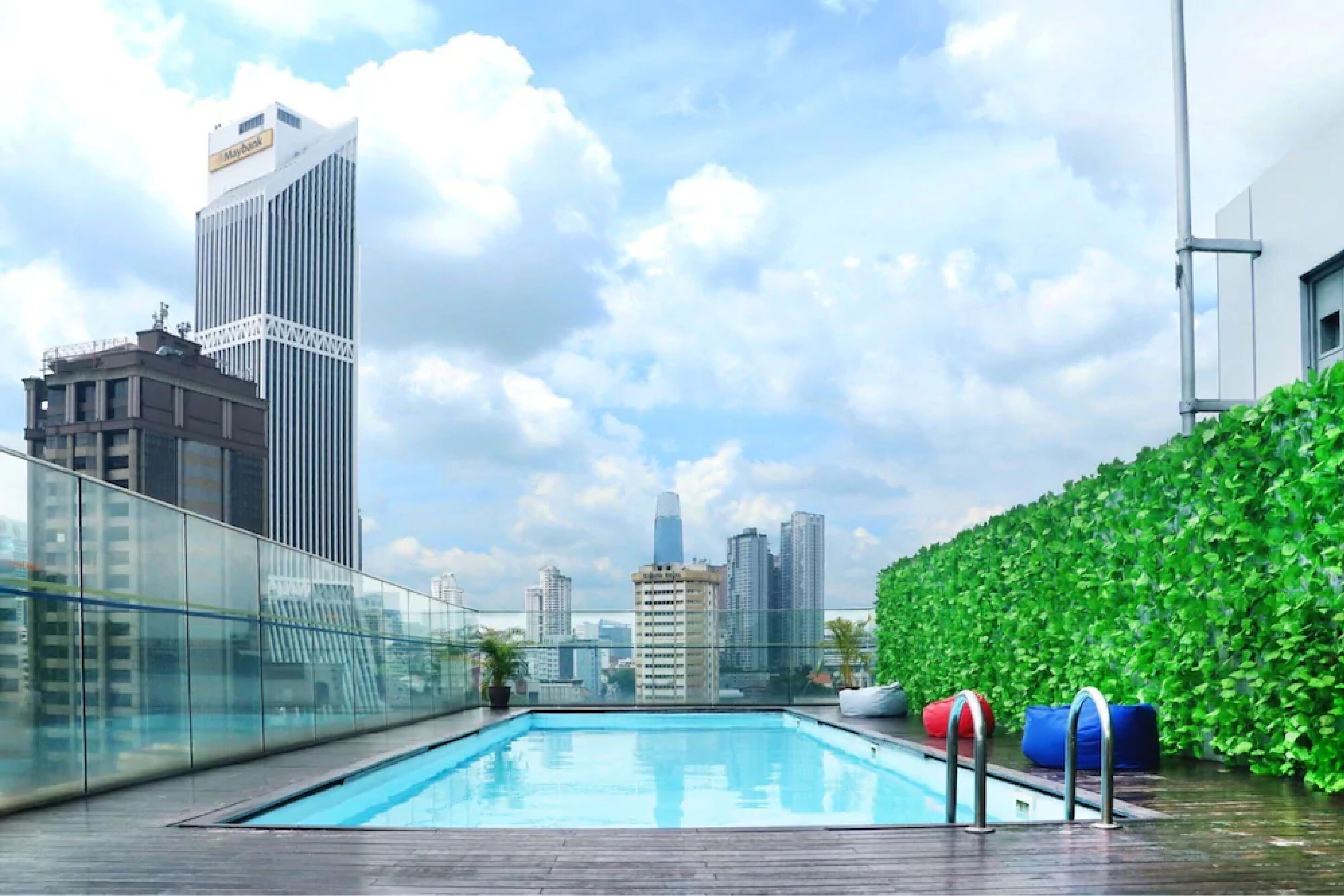 Piscina no terraço com barreira de vidro, sebe verde e paisagem urbana ao fundo.