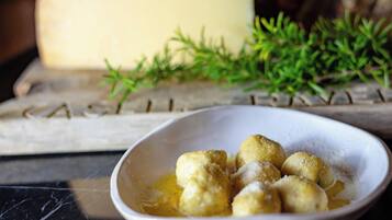 Uma tigela de comida com molho cremoso, um queijo inteiro e vegetação ao fundo.