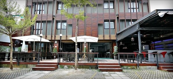 Um edifício moderno com área externa coberta, com mesas e guarda-sóis.
