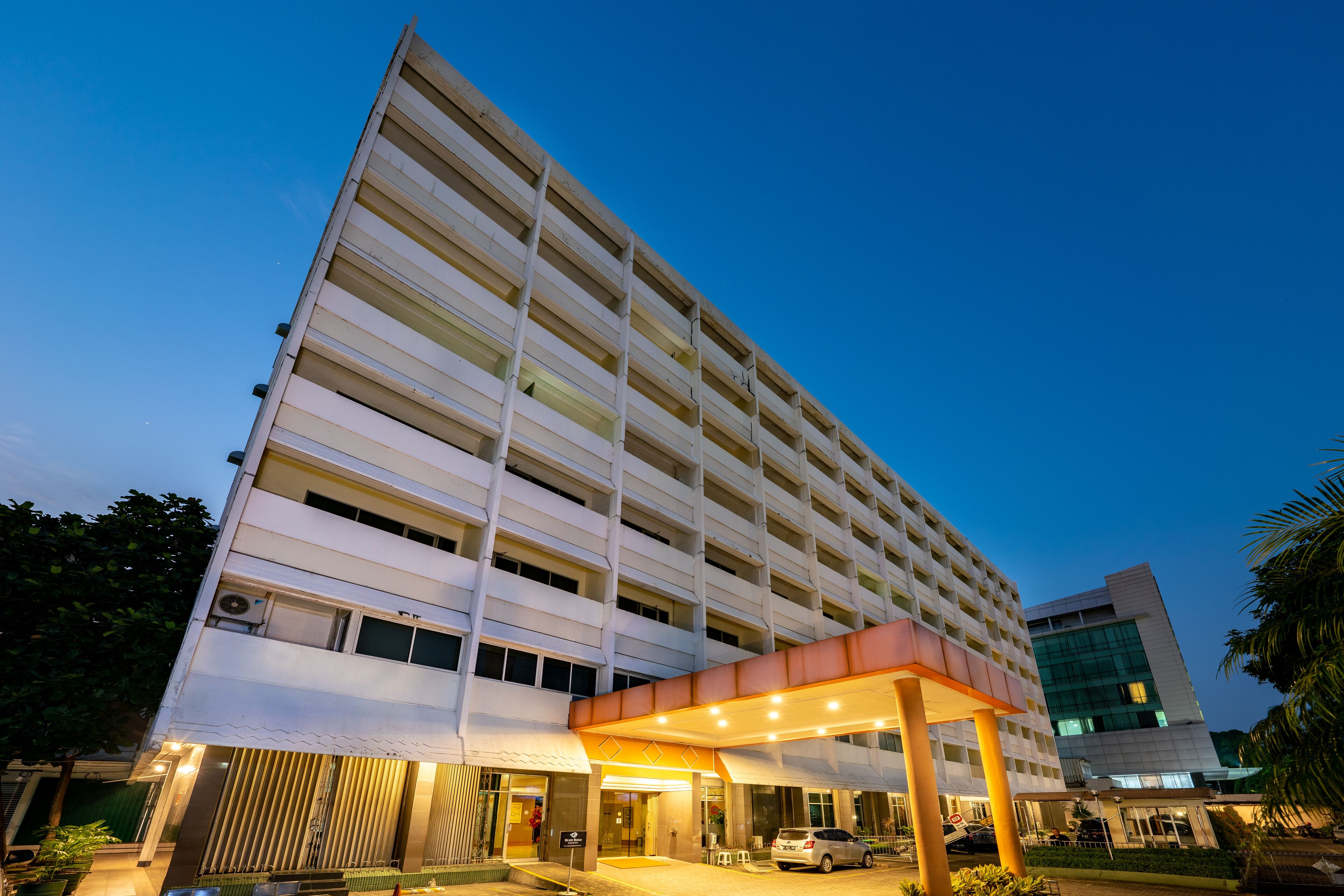 Um hotel de vários andares com design moderno, destacando uma entrada imponente com área coberta e um estacionamento à frente.