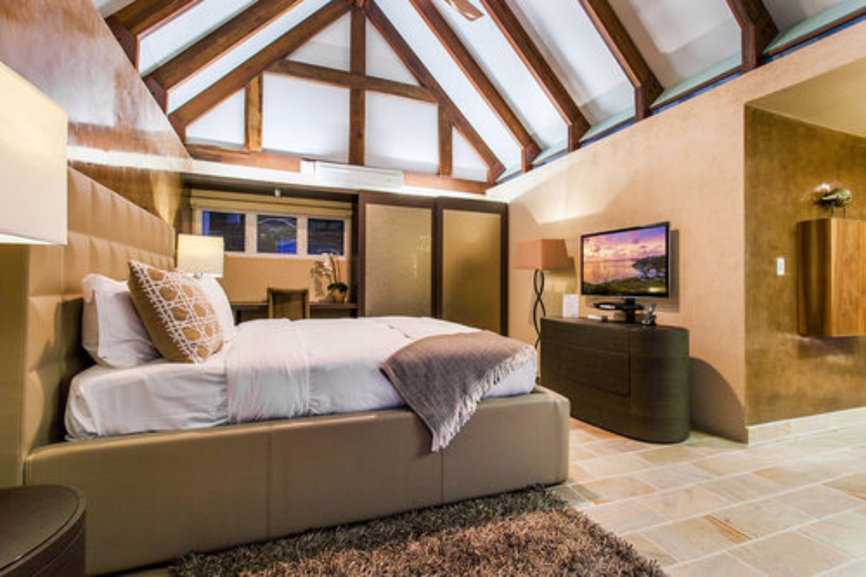 Quarto com uma cama grande, televisão e teto de madeira.