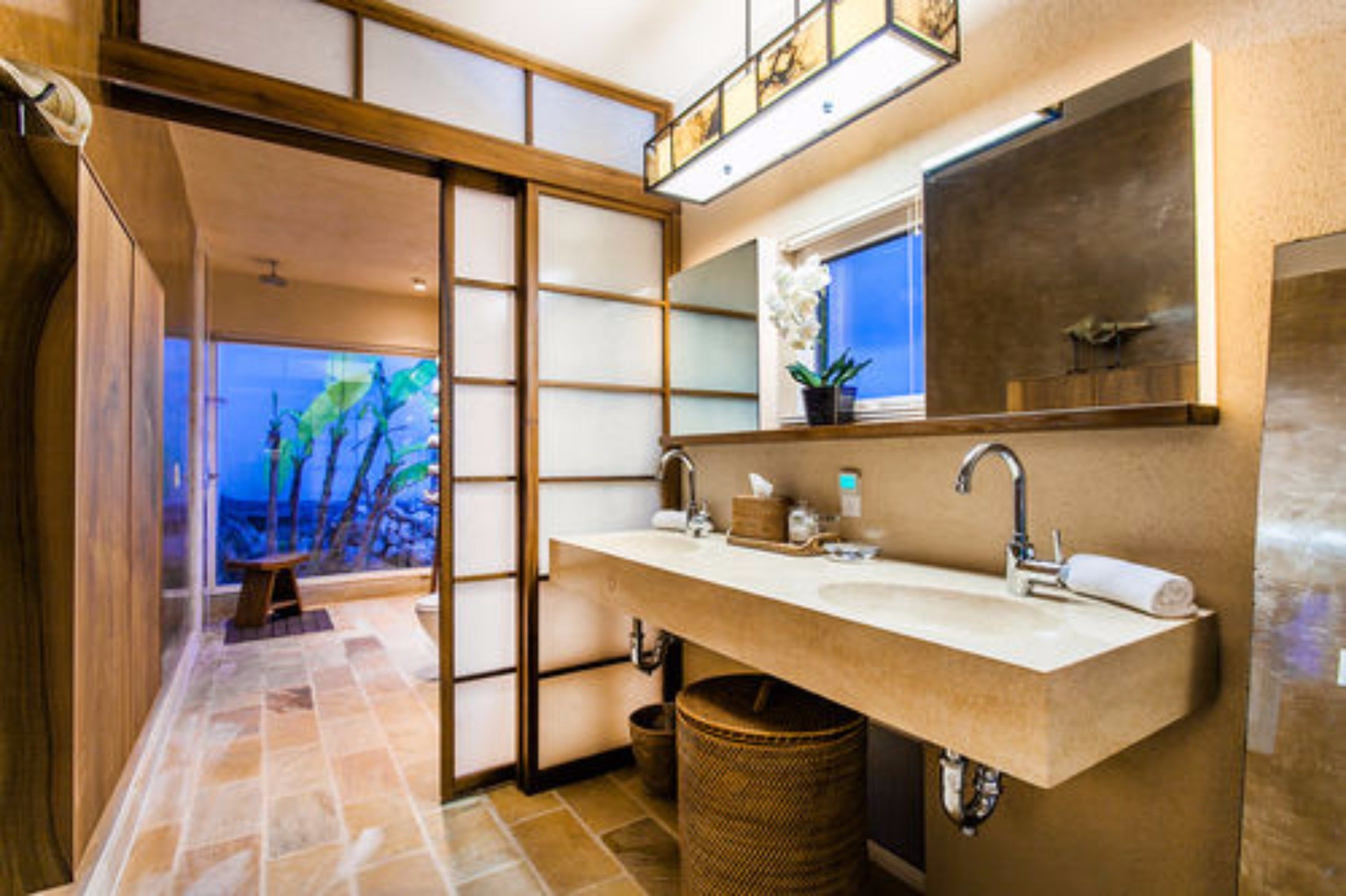 Casa de banho moderna com uma grande pia, um espelho e vista para plantas tropicais.