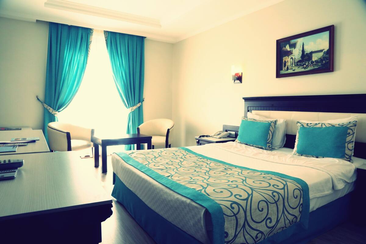 Quarto de hotel com cama, escrivaninha, cadeira e um quadro na parede.