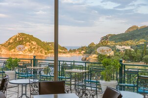 Terraço com mesas ao ar livre, com vista para um lago e colinas.