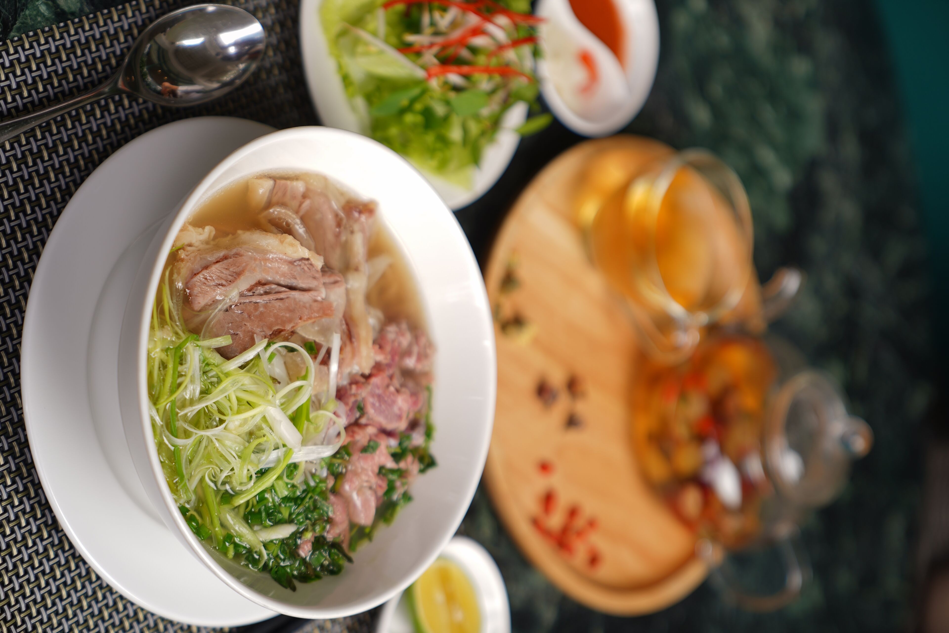 Uma tigela de sopa com carne e legumes, um copo de cerveja e um prato com uma bebida sobre uma mesa.