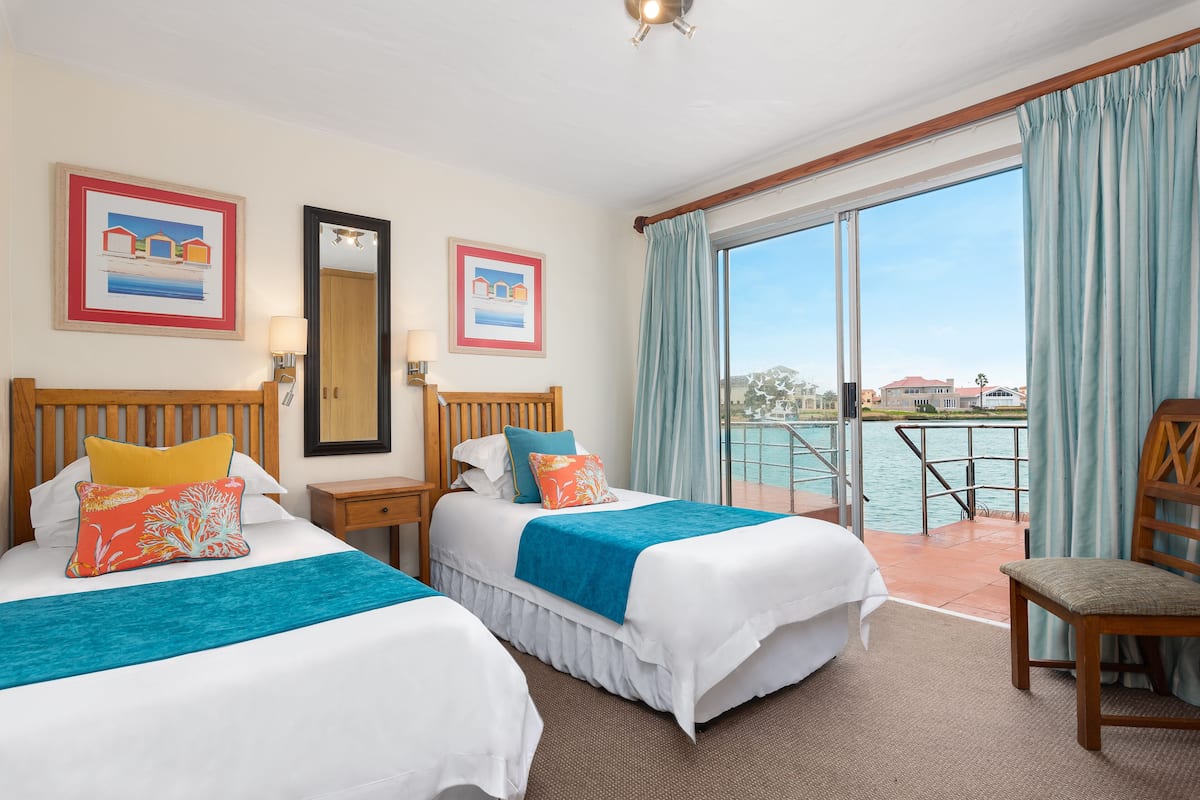 Quarto de hotel com duas camas, varanda com vista para a água e obras de arte nas paredes.