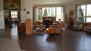 Uma sala de estar espaçosa com lareira, sofás de couro, uma mesa de centro e uma televisão. Há esquis e uma prancha de snowboard encostados na parede.