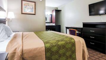 Quarto de hotel com uma cama, uma escrivaninha, um armário, uma televisão e um quadro na parede.