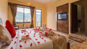 Quarto de hotel com cama, televisão, guarda-roupa e banheiro visível através de uma porta aberta.