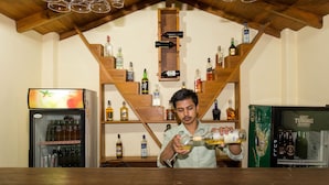 Uma área de bar com teto de madeira, prateleiras com garrafas e um refrigerador.
