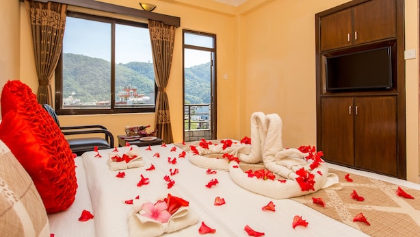 Quarto de hotel com uma cama, um travesseiro vermelho, uma televisão e vista para uma montanha.