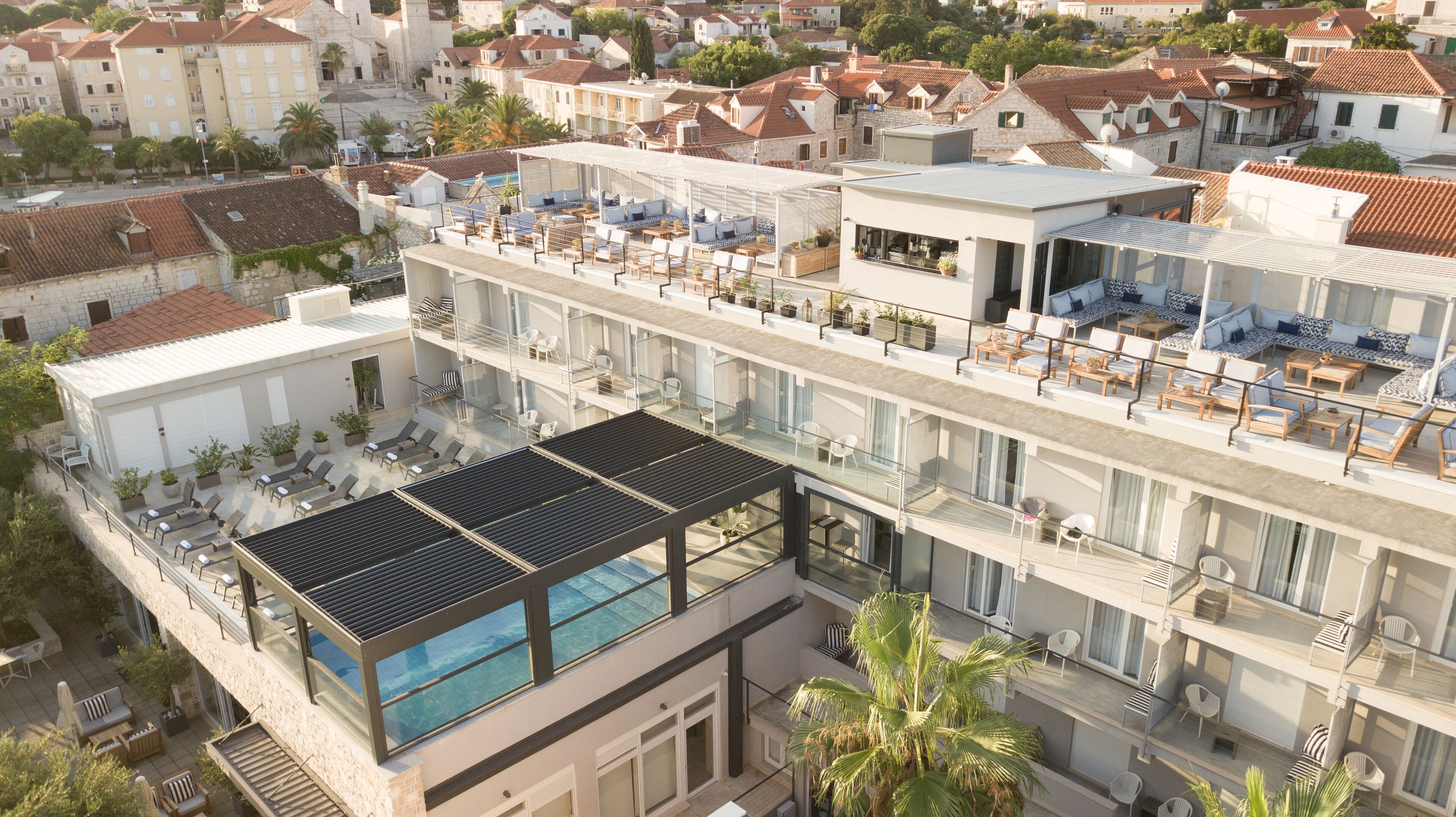 Um hotel com vários andares, piscina no terraço, áreas de estar ao ar livre e vista do bairro ao redor.